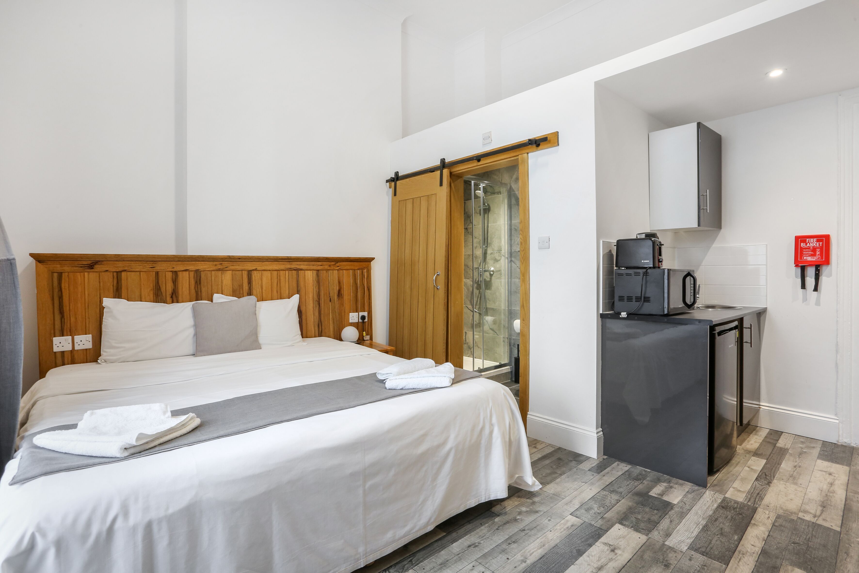 Quarto de hotel com uma cama, uma pequena cozinha e uma porta de correr, além de um alarme de incêndio.