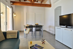 Uma sala de estar moderna com um sofá, uma mesa de centro com uma revista e um copo de suco de laranja, uma TV e uma área de jantar com cadeiras e uma mesa.