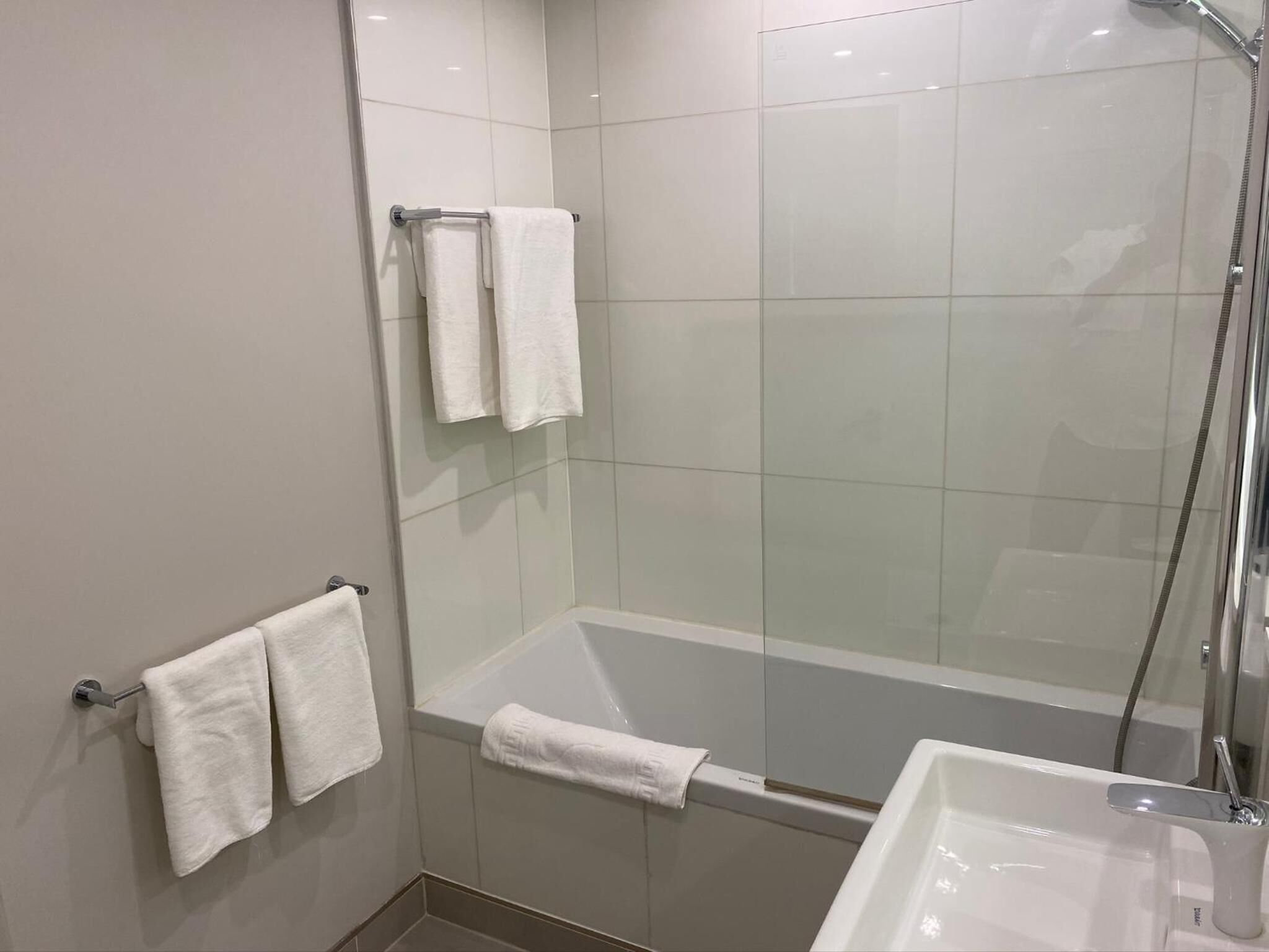 Casa de banho moderna com chuveiro em cabine de vidro, banheira e dois porta-toalhas com toalhas brancas.