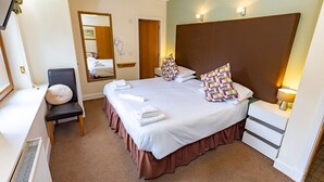 Quarto de hotel bem arrumado com uma cama grande, uma cadeira, uma mesinha de cabeceira e um espelho.