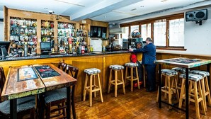 Um bar com móveis de madeira, um bartender e diversas garrafas de bebidas alcoólicas.