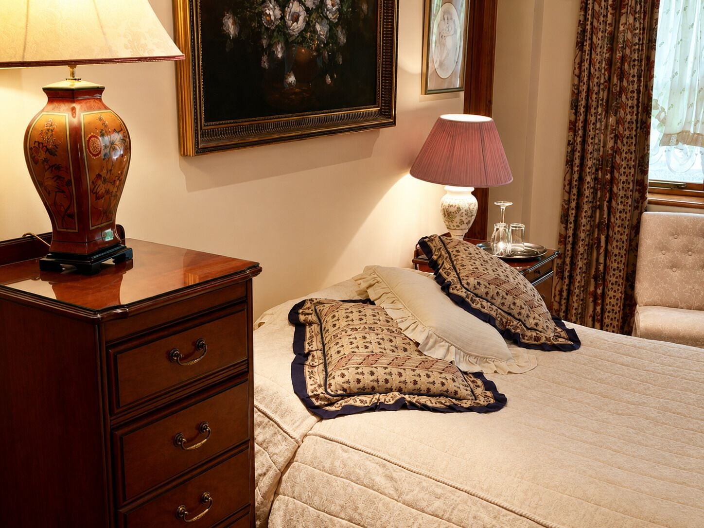 Quarto bem arrumado com mesa de cabeceira de madeira, cama com roupa de cama estampada, quadro na parede e janela com cortinas.