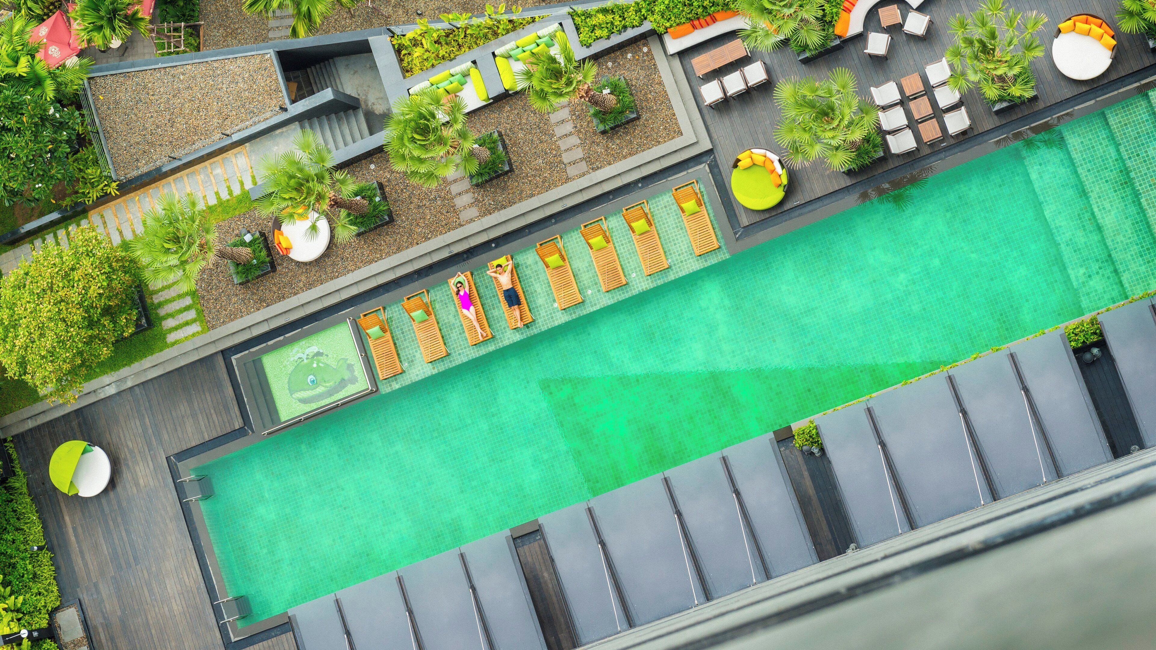 Vista aérea de uma área de piscina de hotel com vários espreguiçadeiras e uma piscina central.