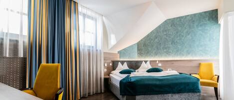 Quarto de hotel moderno com uma cama, duas cadeiras amarelas, uma mesa e uma janela grande com cortinas.