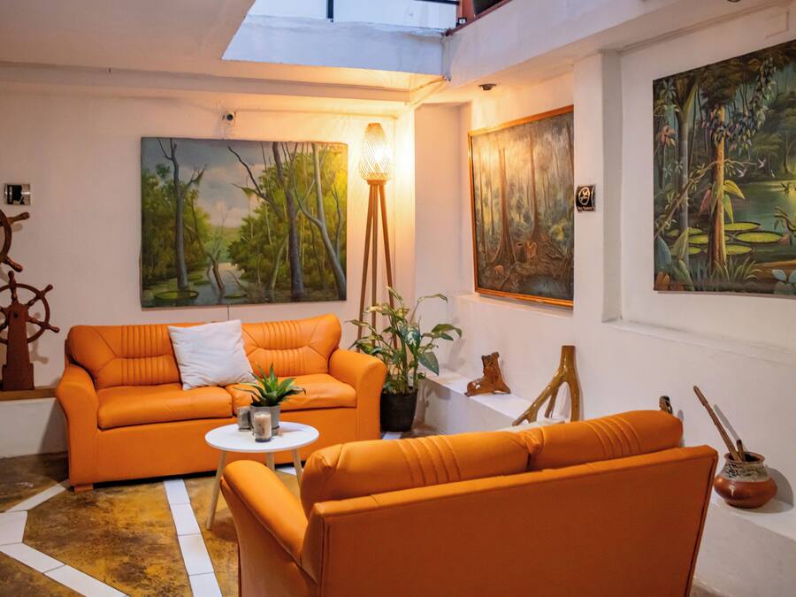 Uma sala de estar com um sofá laranja, uma mesa redonda pequena e duas pinturas na parede.
