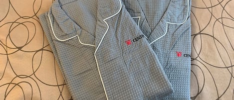 Dois conjuntos de pijama cinza dobrados, com detalhes em branco e um logotipo vermelho sobre um tecido estampado.