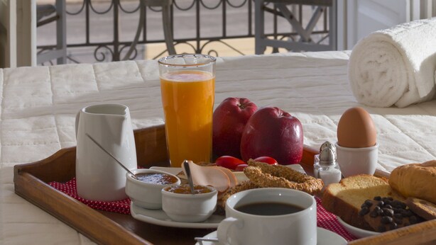 Uma bandeja de café da manhã com café, ovos, torradas e frutas numa varanda com vista para o mar.