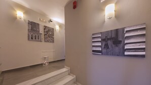 Uma escadaria com piso e paredes em tons claros, conduzindo a um quarto com uma porta branca.