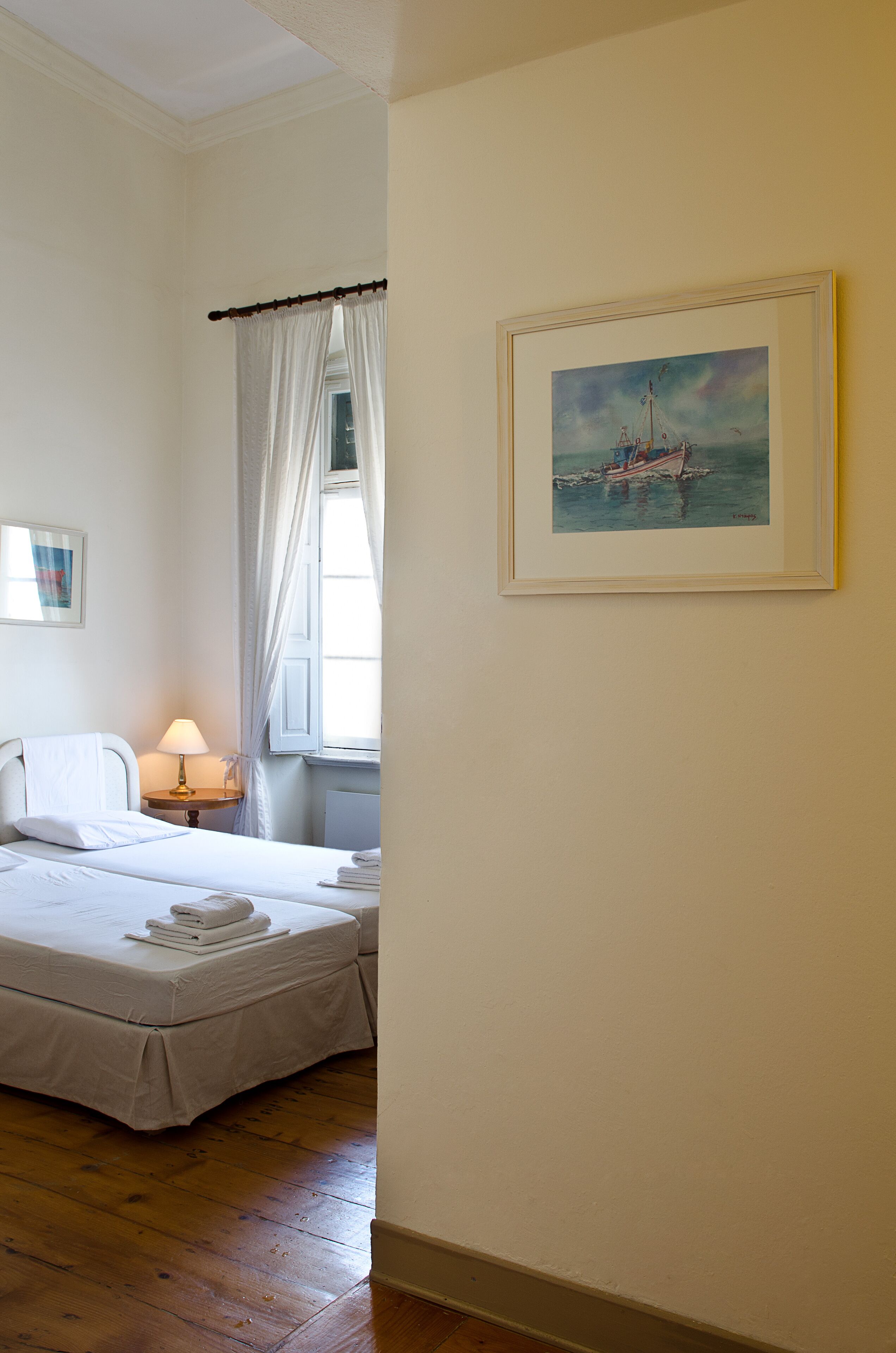 Quarto de hotel com cama, luminária de cabeceira, janela com cortinas e um quadro pendurado na parede.
