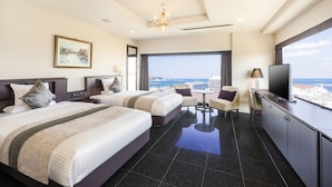 Quarto de hotel com duas camas, televisão, secretária e vista para o mar.