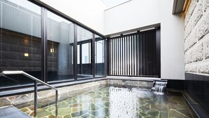 Piscina interior moderna com água cristalina, azulejos de pedra e parede de vidro.