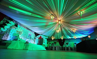 Um palco com tecido drapeado e lanternas penduradas, um espelho e uma mesa coberta por um pano branco.