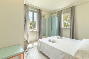 Quarto de hotel com cama, uma pequena mesa, guarda-roupa e janela com cortinas.