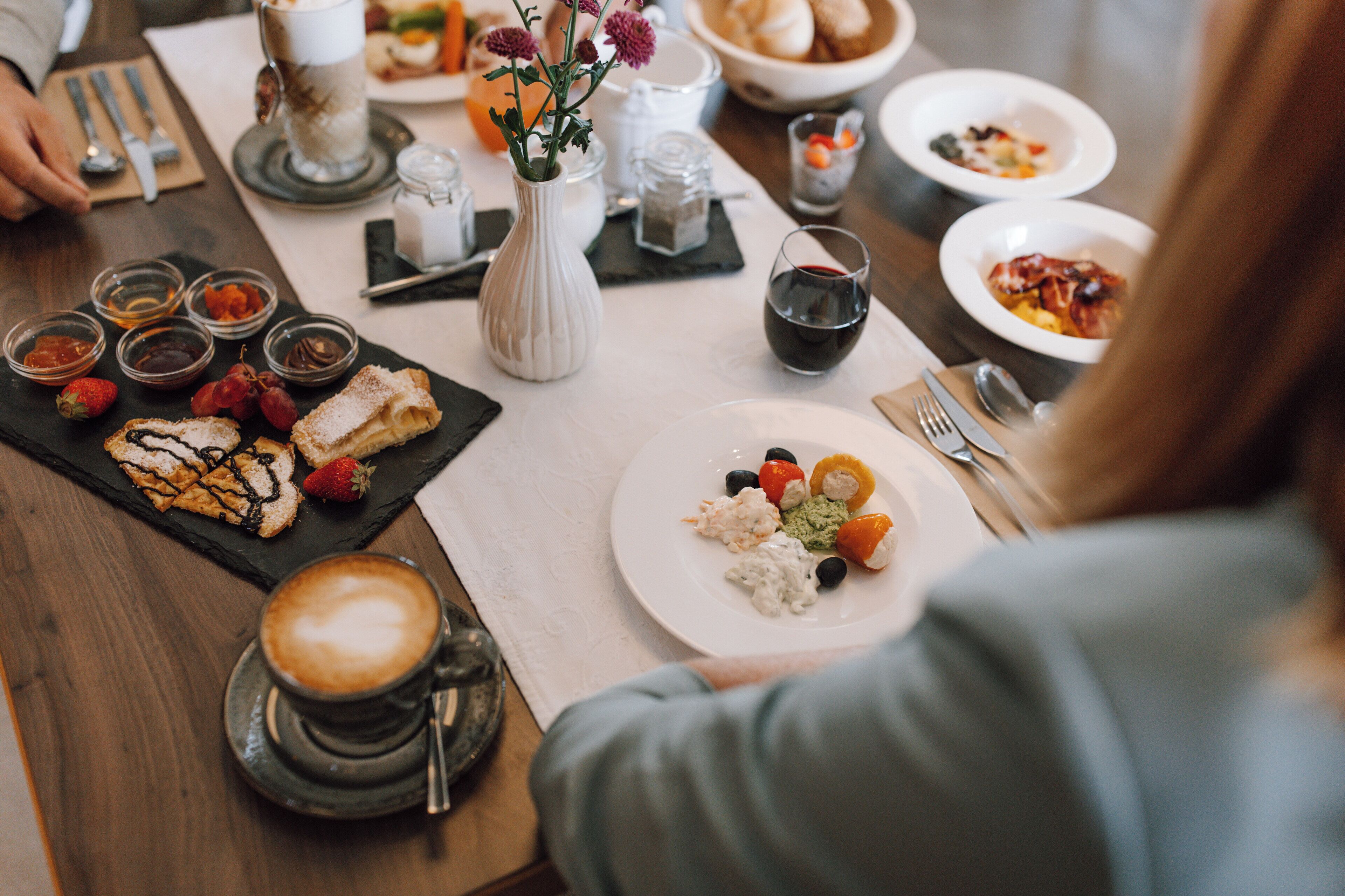 Uma mesa de jantar posta com diversos pratos, uma xícara de café e um vaso com flores.