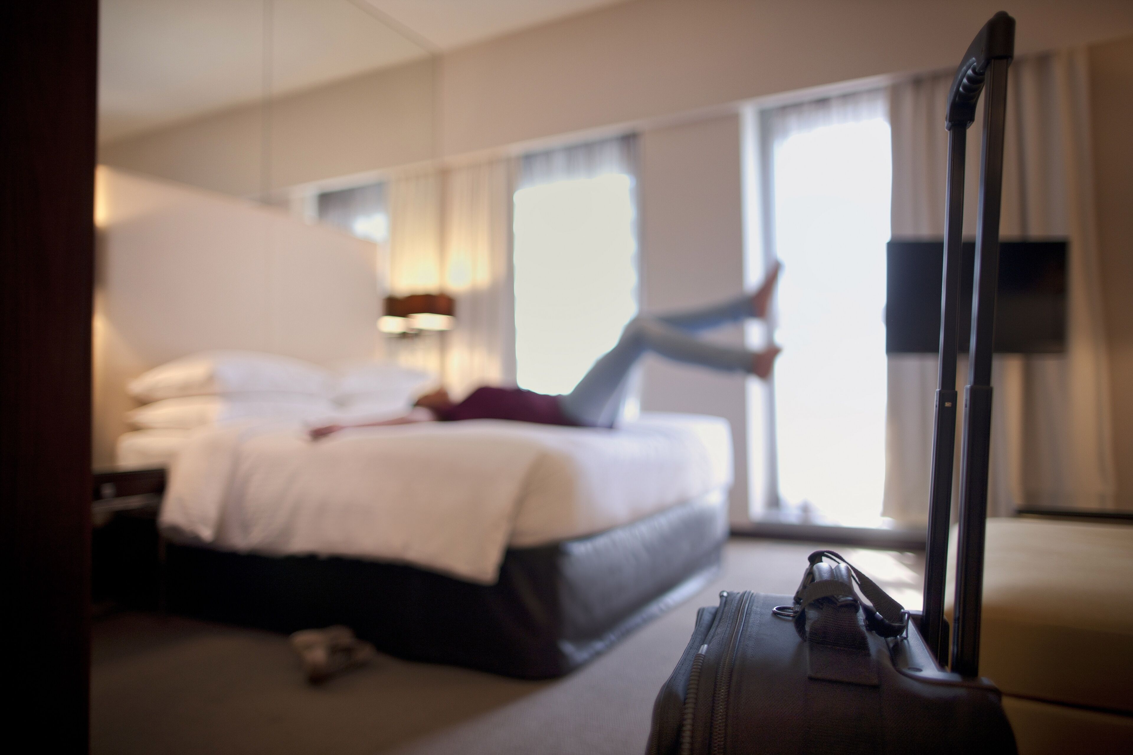 Quarto de hotel com uma cama, uma mala e uma janela com cortinas.
