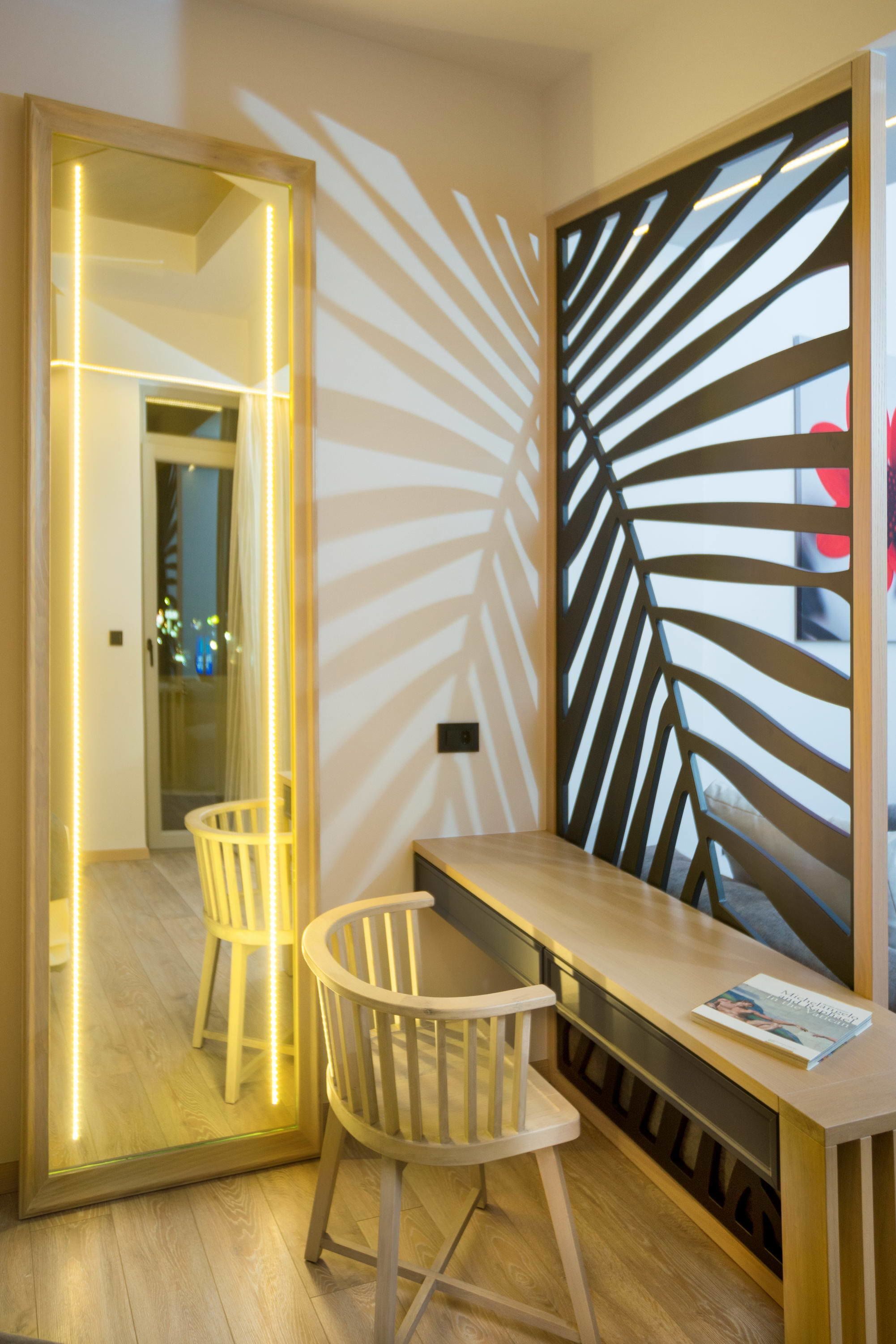 Quarto moderno com escrivaninha de madeira, duas cadeiras brancas, um espelho grande e um painel decorativo na parede.