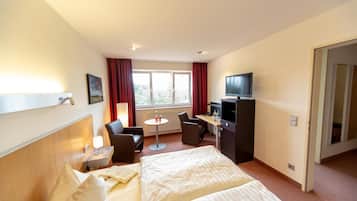 Quarto de hotel com cama, escrivaninha, cadeira, televisão e janela com cortinas.