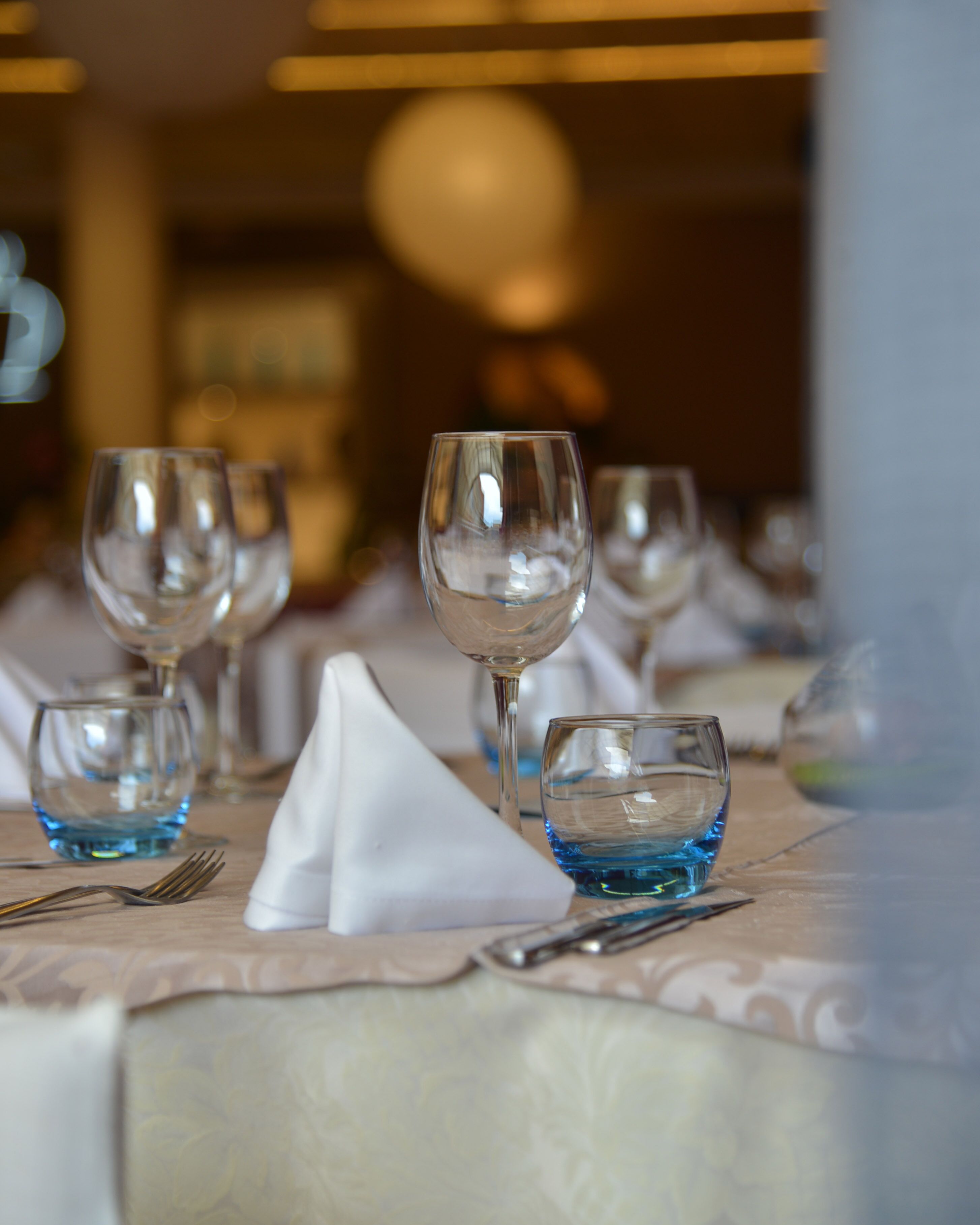 Uma mesa de jantar posta com vários copos de vinho e um copo de água azul, com um guardanapo dobrado ao centro.
