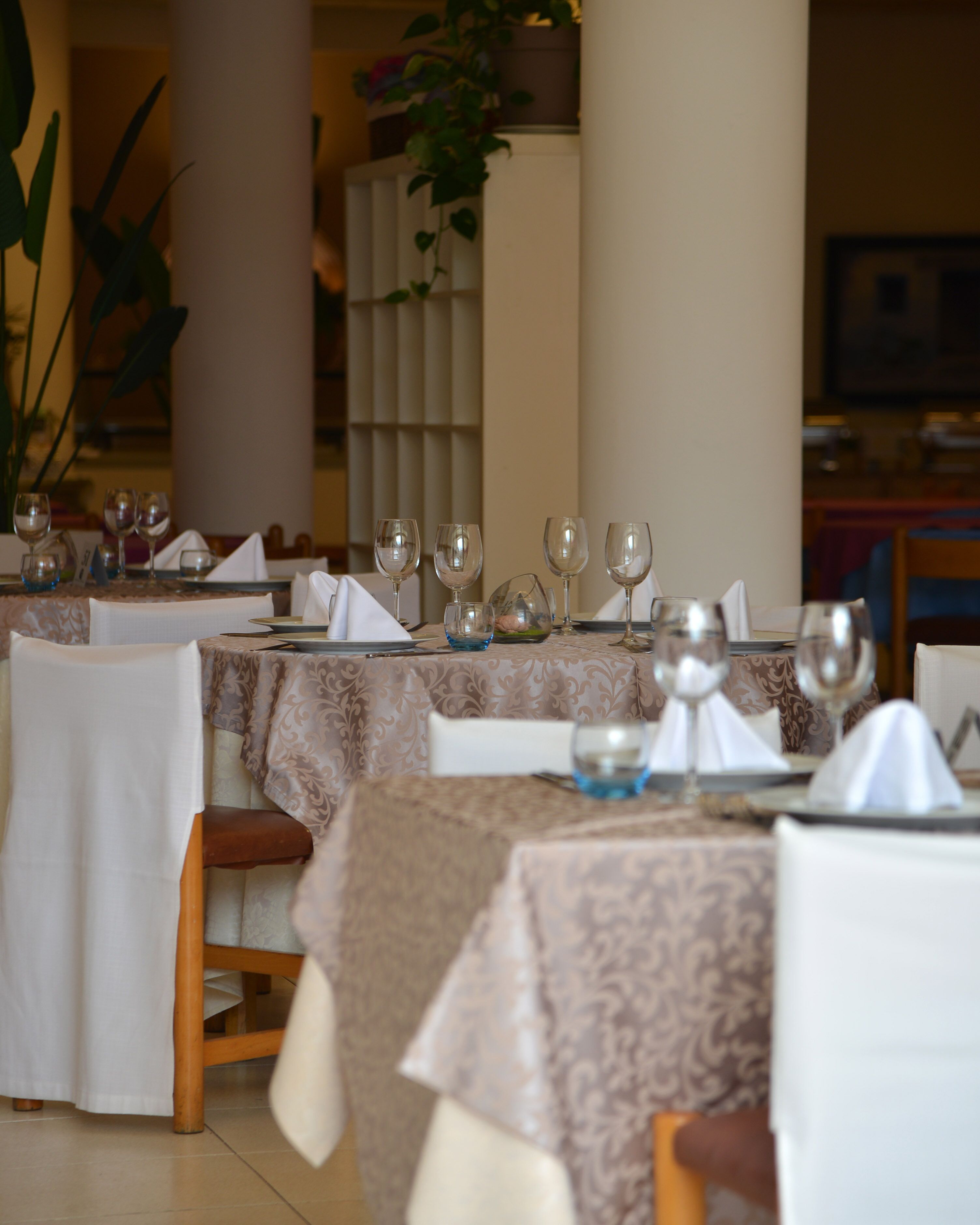 Restaurante com várias mesas preparadas para refeições, com toalhas de mesa brancas e estampadas, e uma variedade de copos.
