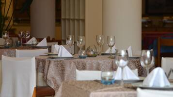 Restaurante com várias mesas preparadas para refeições, com toalhas de mesa brancas e estampadas, e uma variedade de copos.