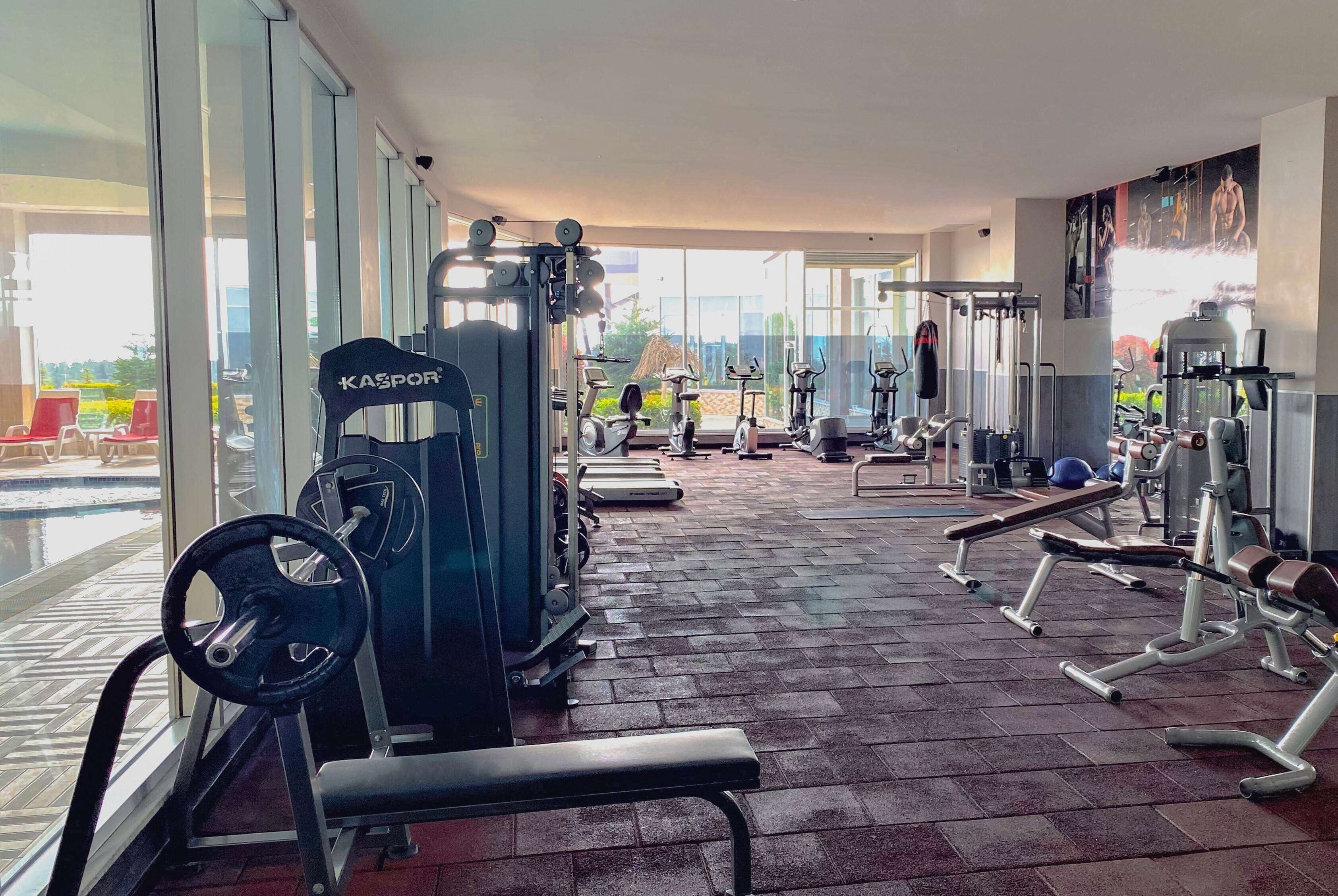 Uma academia com diversos equipamentos de exercício, incluindo aparelhos de musculação e equipamentos de cardio, dispostos em um espaço amplo com grandes janelas.