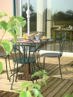 Um pátio externo com mesa e cadeiras, um deck de madeira e vista da região ao redor.