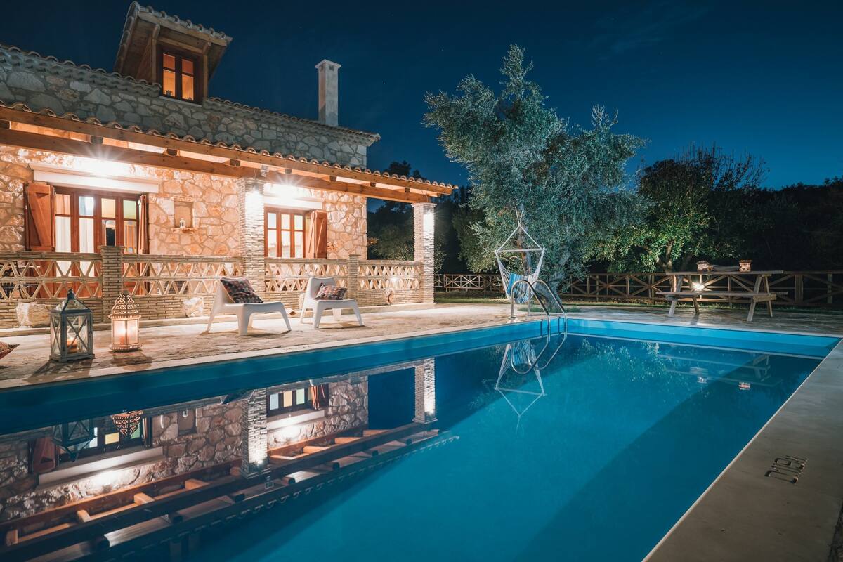 Um edifício de pedra com piscina, área de estar externa e uma rede.