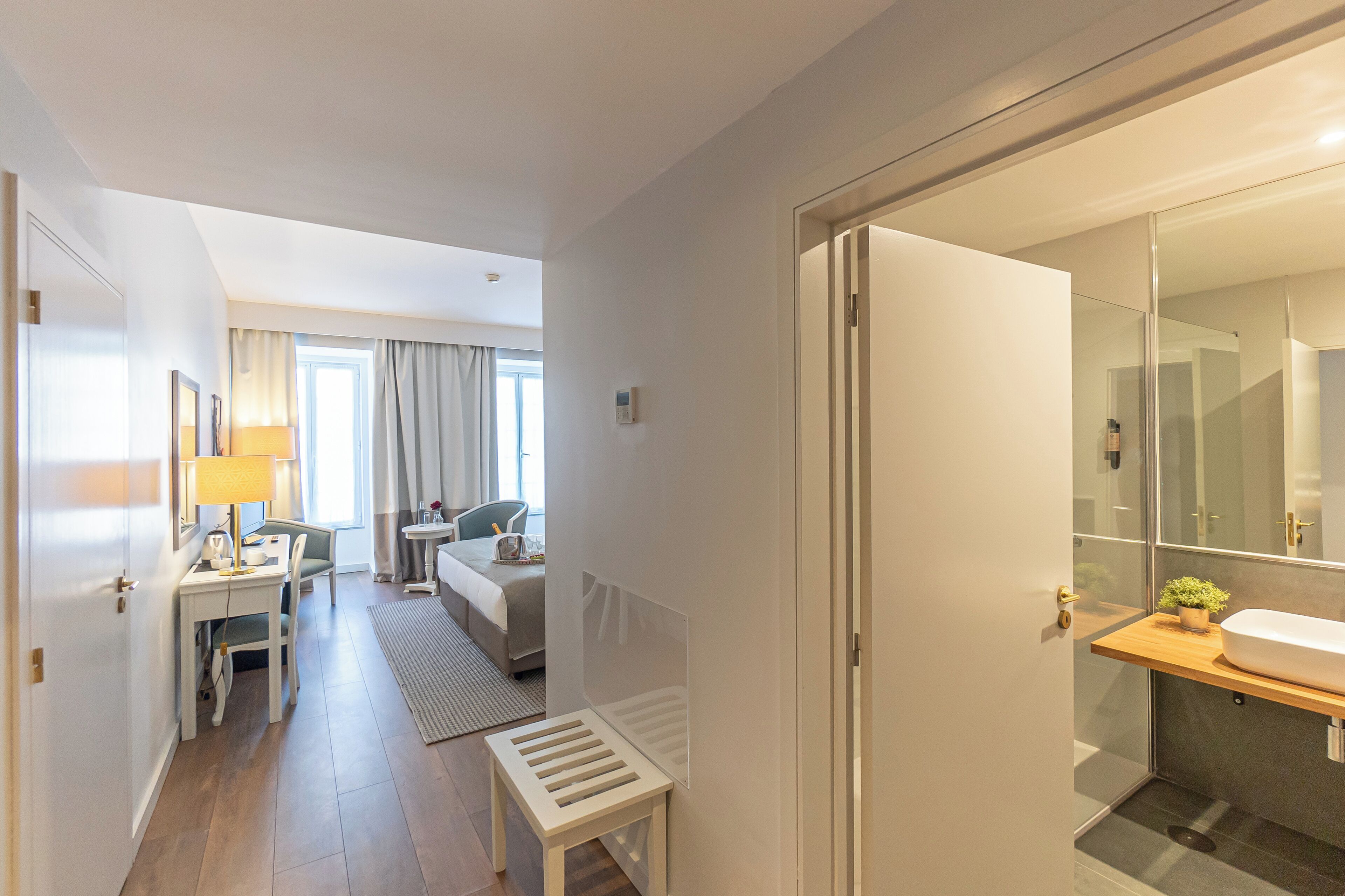 Quarto de hotel com escrivaninha, cadeira, cama e banheiro com pia e espelho.