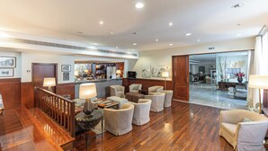 Um hall amplo com piso de madeira, vários espaços de estar, um bar e vista para outro ambiente.