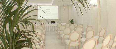 Sala de conferências com cadeiras brancas e tela de projeção.
