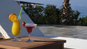 Uma mesa de madeira com duas bebidas, uma palmeira e vista para o mar.
