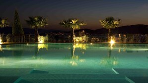 Área de piscina à noite, com palmeiras e vista para a cidade ao fundo.