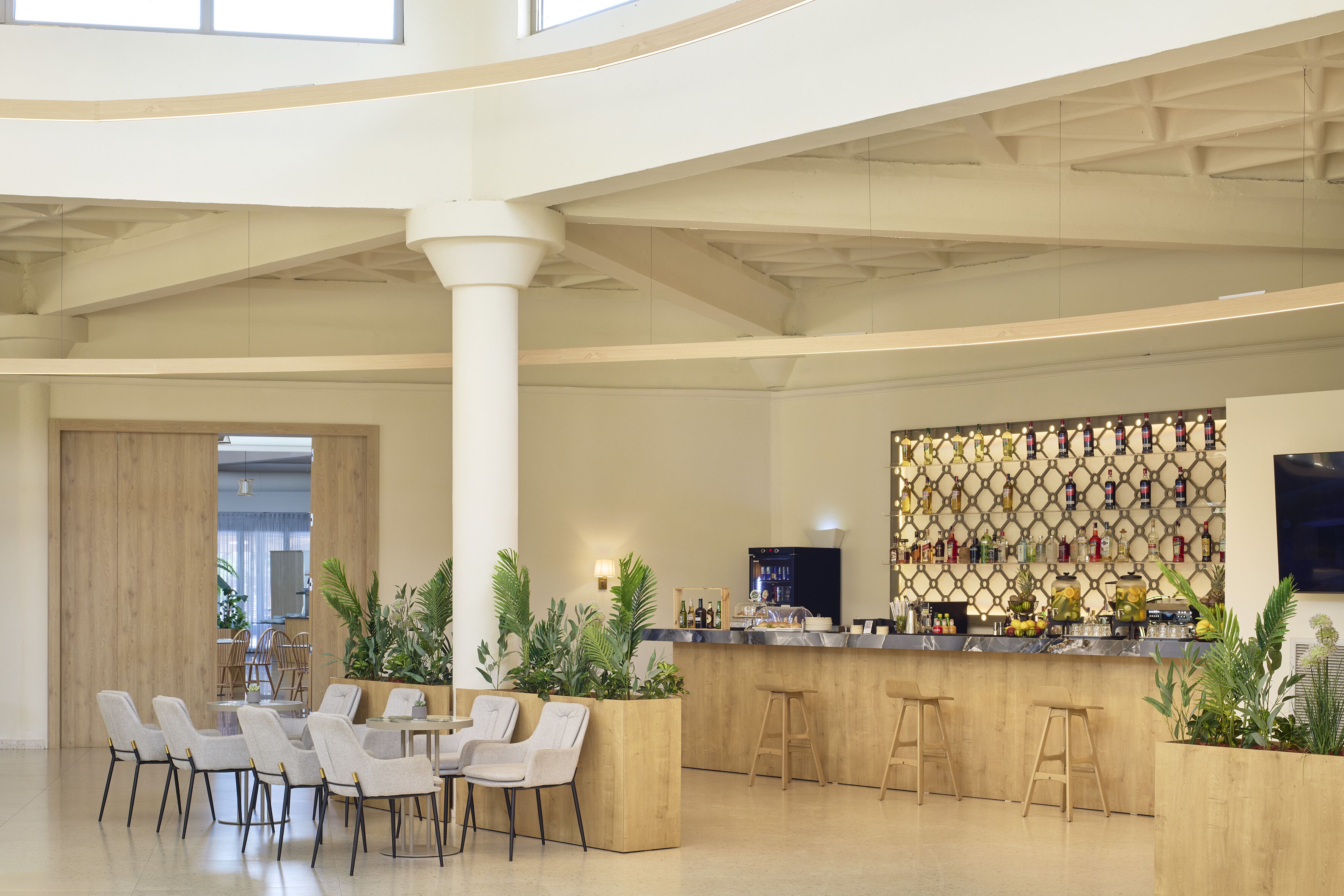 Um hall espaçoso com teto alto, uma coluna central, área de bar com banquetas e espaço de estar com mesas e cadeiras.