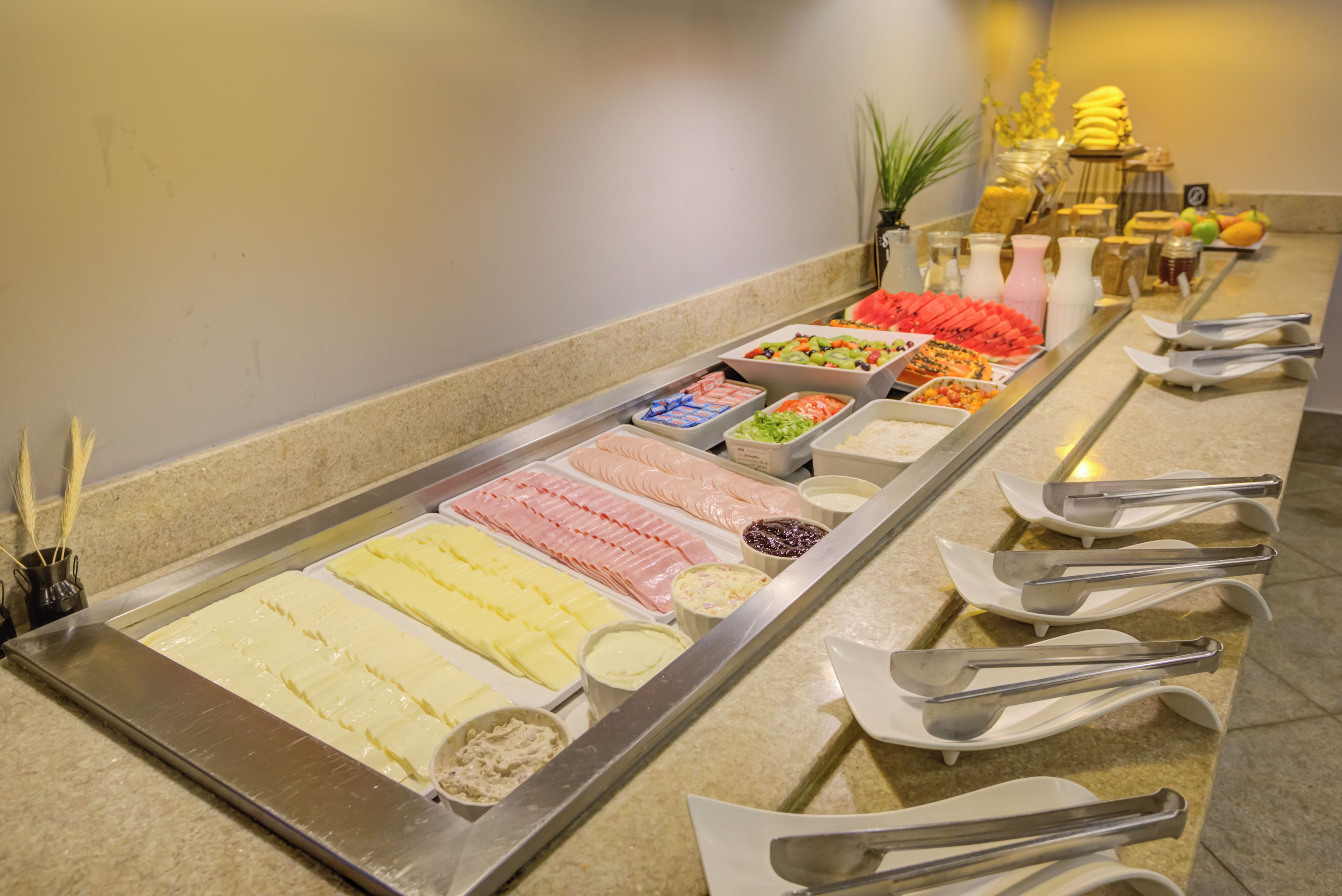 Buffet com diversas opções de comida e utensílios dispostos em um balcão.