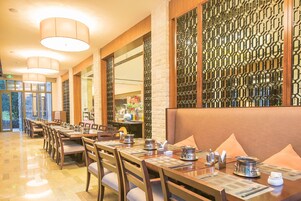 Restaurante com várias mesas, cadeiras e um painel decorativo.