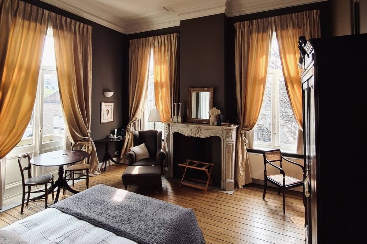 Quarto de hotel com uma cama grande, uma escrivaninha, uma cadeira e uma lareira.