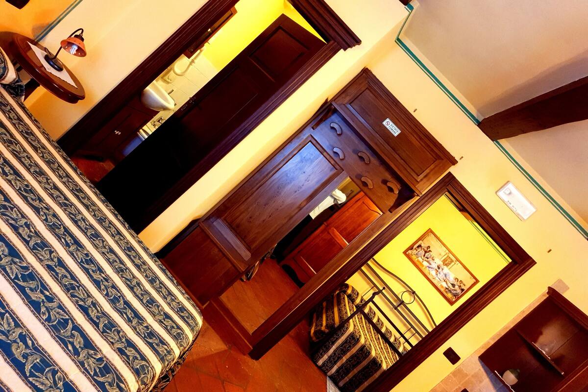 Um quarto com uma cama estampada, porta de madeira, escada e um quadro na parede.