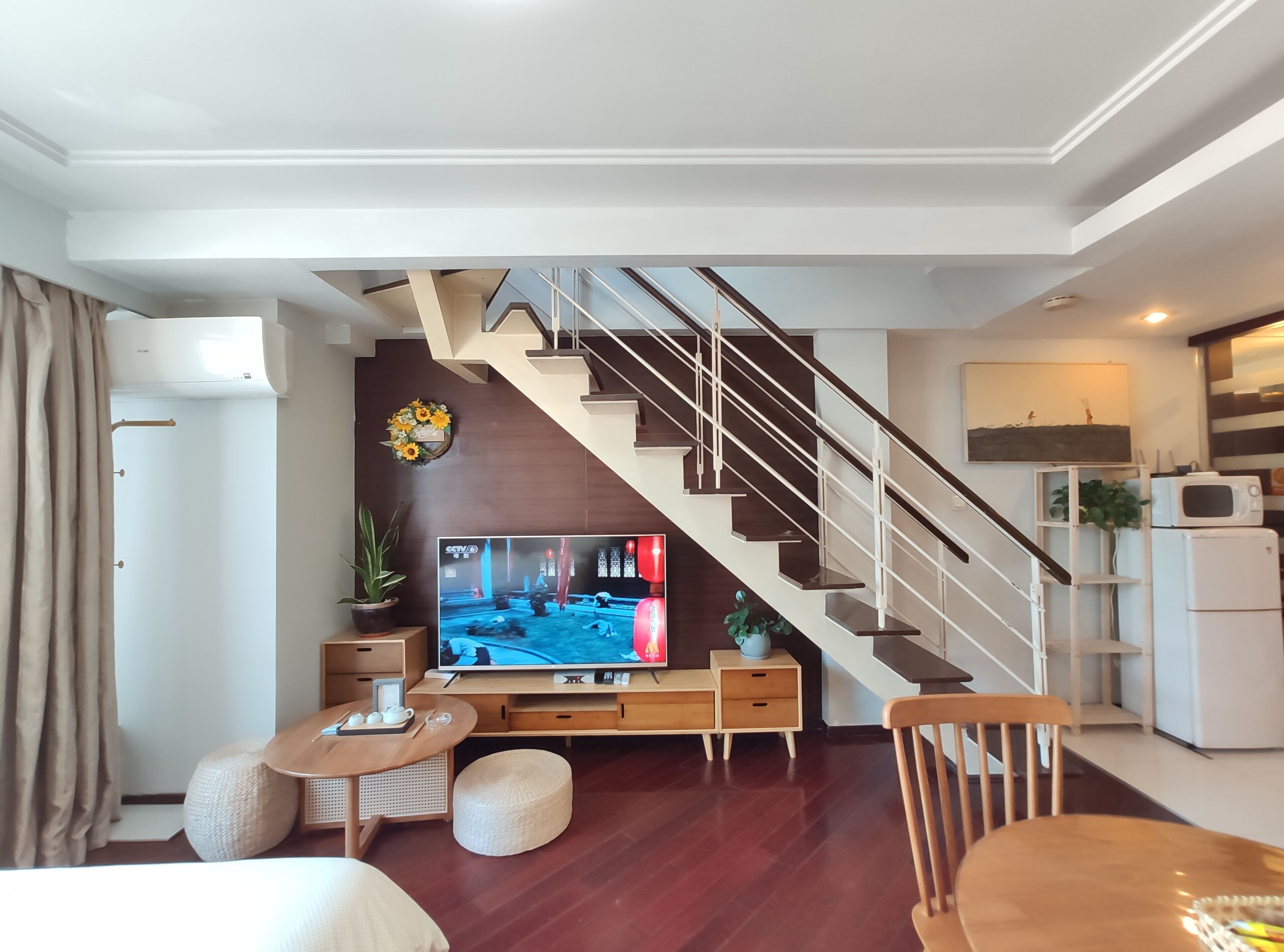 Uma sala de estar moderna com televisão de tela plana, móveis de madeira, uma escada e uma área de cozinha.