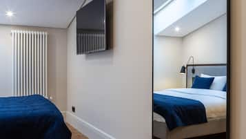 Quarto moderno com um espelho grande, uma cama com roupa de cama azul, uma televisão fixada na parede e piso de madeira em padrão herringbone.
