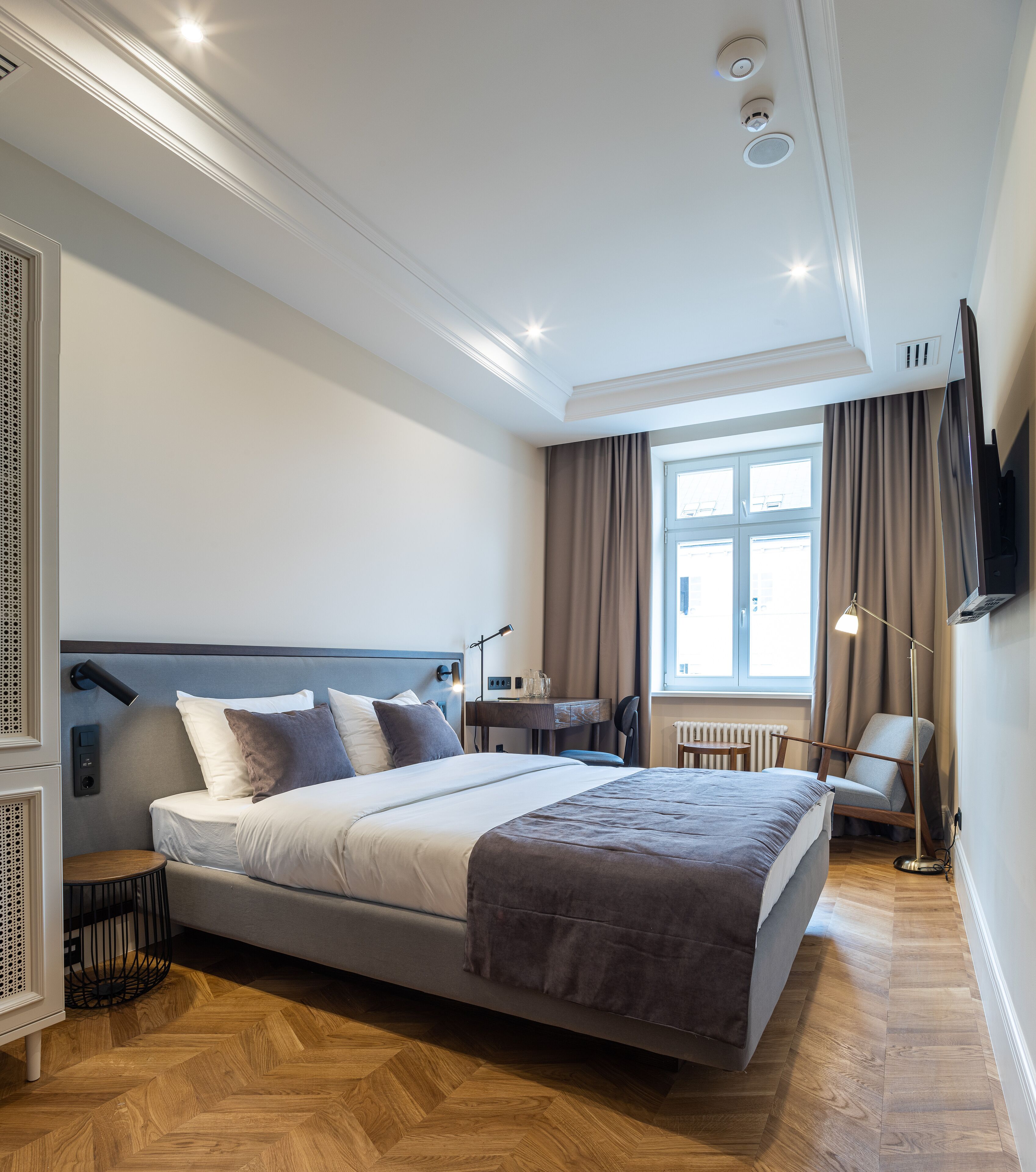 Quarto de hotel moderno com uma cama grande, uma escrivaninha, uma cadeira e uma TV fixada na parede.