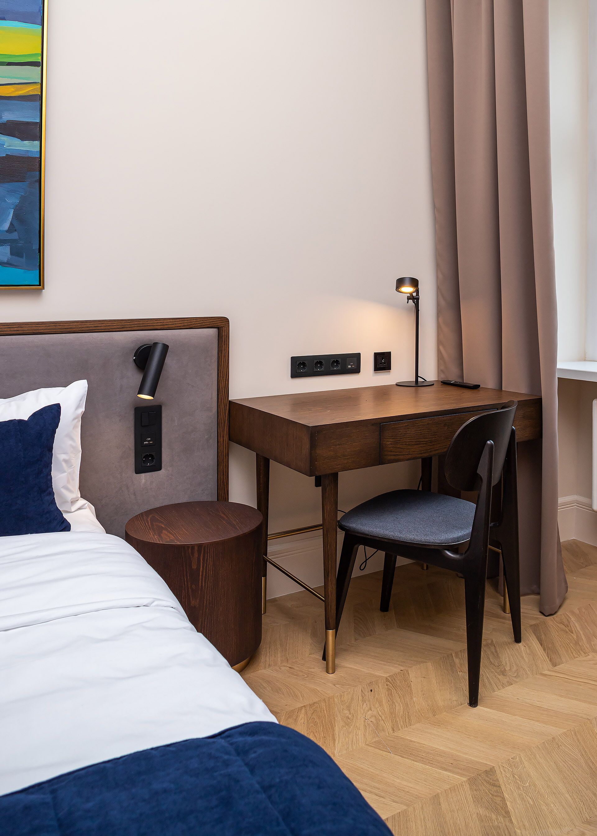 Quarto de hotel com cama, escrivaninha, cadeira e luminária.