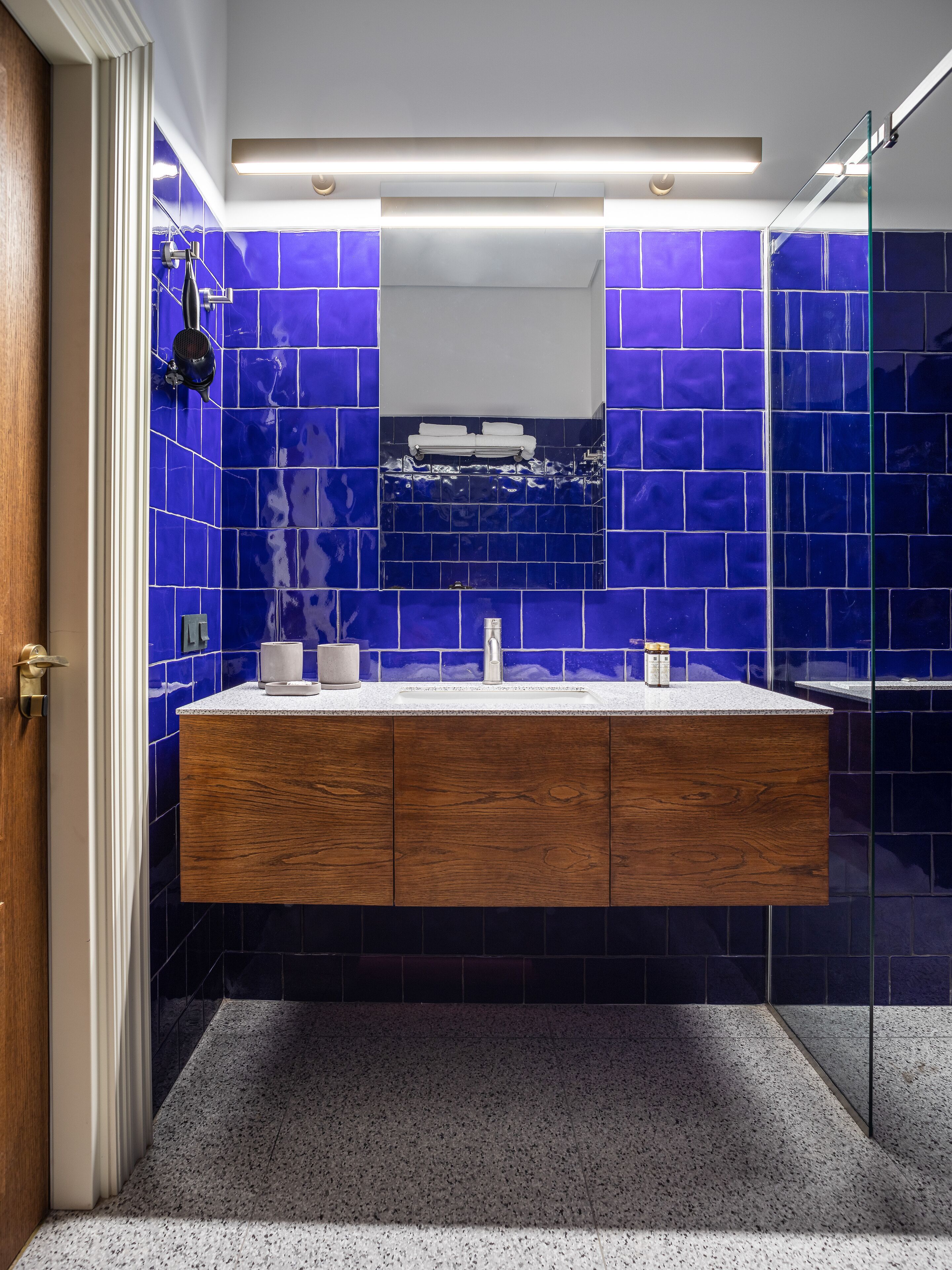 Uma casa de banho moderna com azulejos azuis, um lavatório de madeira, cabine de duche em vidro e uma sanita branca.