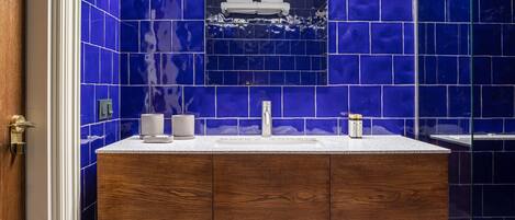 Uma casa de banho moderna com azulejos azuis, um lavatório de madeira, cabine de duche em vidro e uma sanita branca.