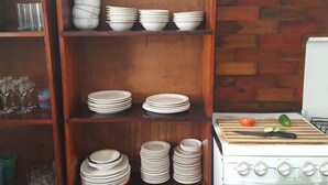 Uma cozinha com prateleiras de madeira contendo pratos e tigelas, um fogão e uma tábua de corte com legumes.