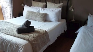 Uma cama bem arrumada com lençóis brancos, um cobertor bege e uma toalha enrolada. Há duas luminárias de cabeceira em uma mesinha de noite.