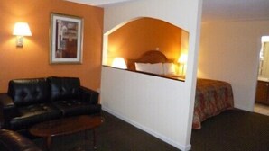 Quarto de hotel com um sofá de couro preto, uma pequena mesa de madeira, uma divisória branca e uma cama com colcha estampada.