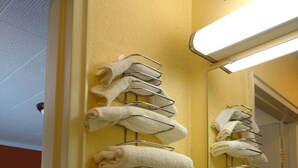 Casa de banho com paredes amarelas, um espelho e um porta-toalhas com vários toalhas.