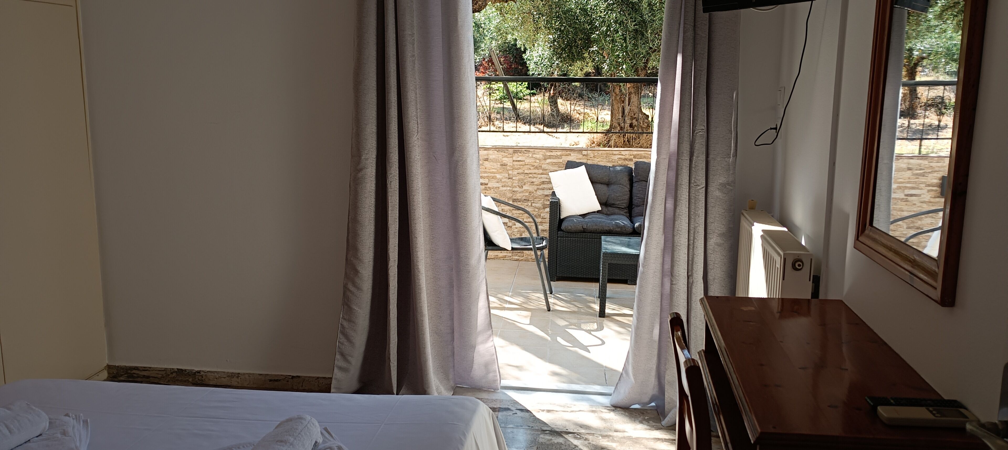 Quarto de hotel com uma cama, uma escrivaninha de madeira e vista para uma área de estar externa.