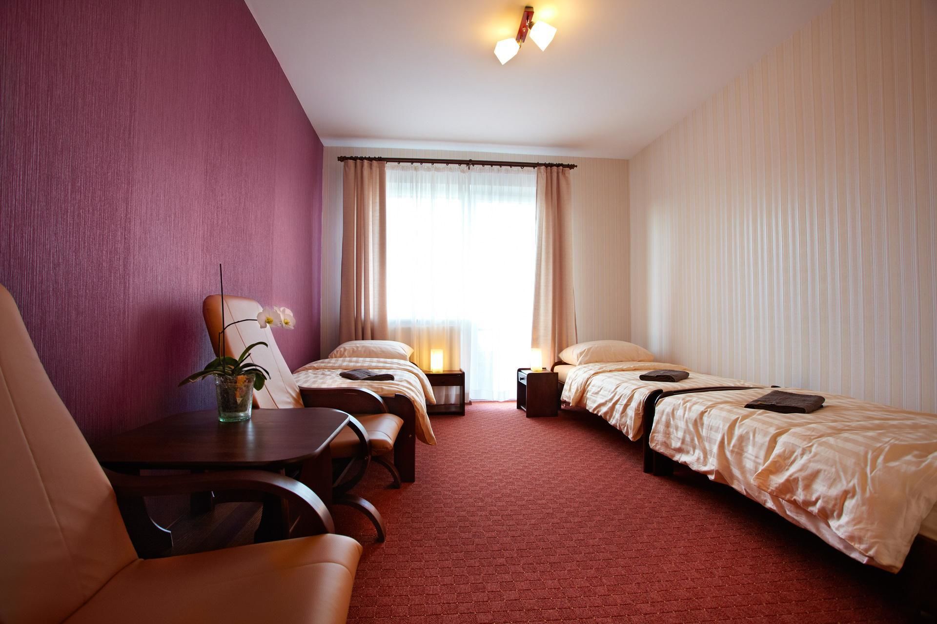 Quarto de hotel com duas camas, uma escrivaninha com cadeira, um vaso com flores e uma janela com cortinas.