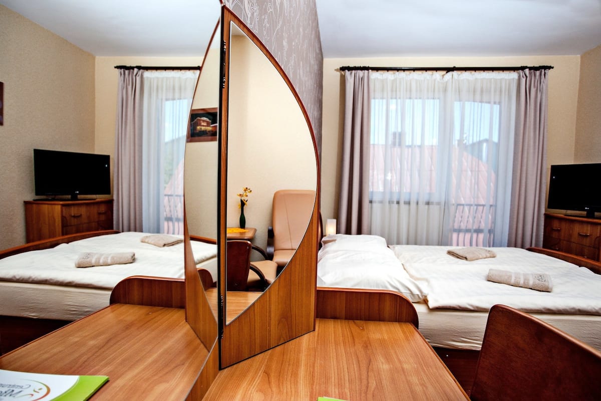 Quarto de hotel com duas camas, uma secretária de madeira, uma cadeira, uma TV e um espelho.